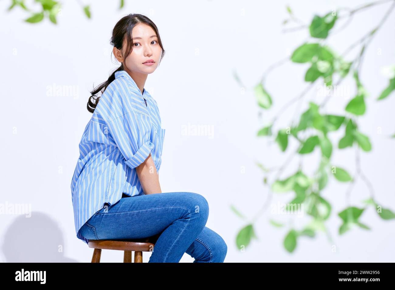 A woman sitting on a stool with a blue shirt and jeans Stock Photo - Alamy