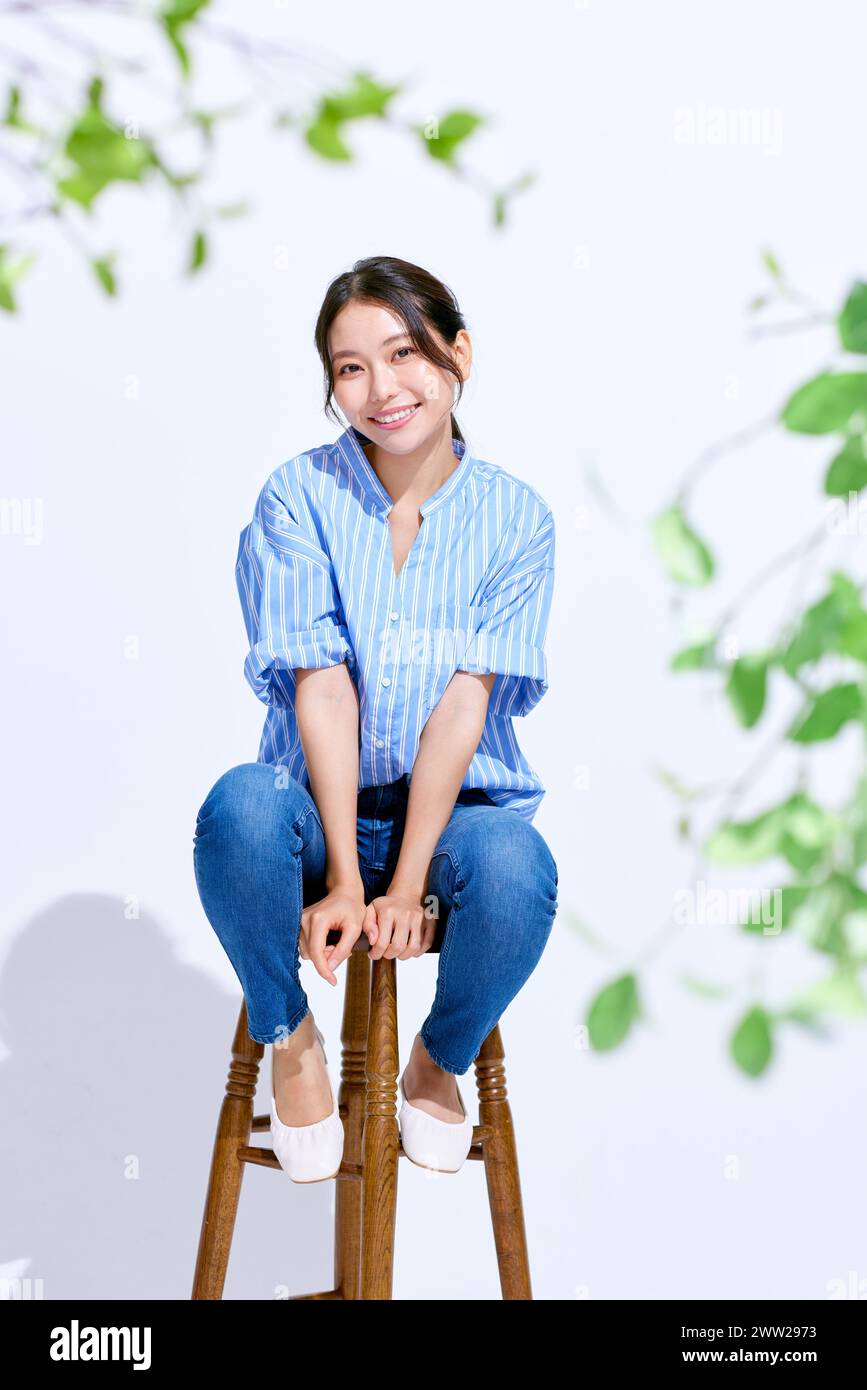 Asian woman sitting on stool with green plant in background Stock Photo ...