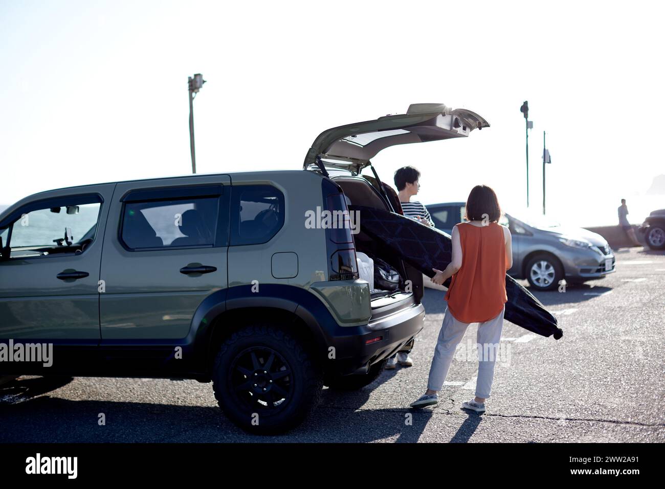 A woman and a man loading a surfboard into the trunk of a car Stock ...