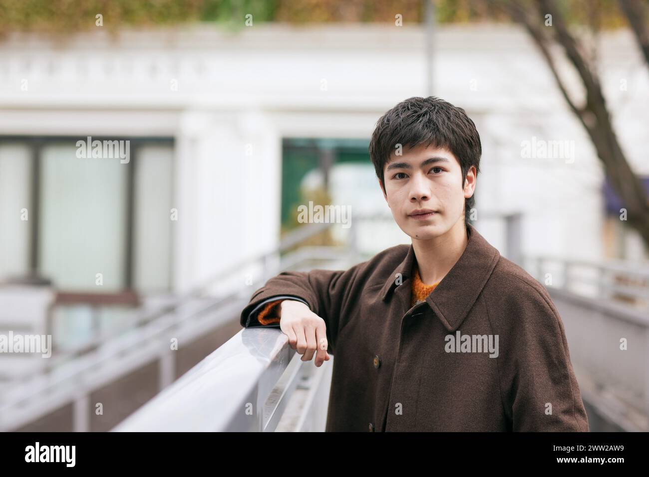 Young man in brown coat leaning on ledge Stock Photo - Alamy