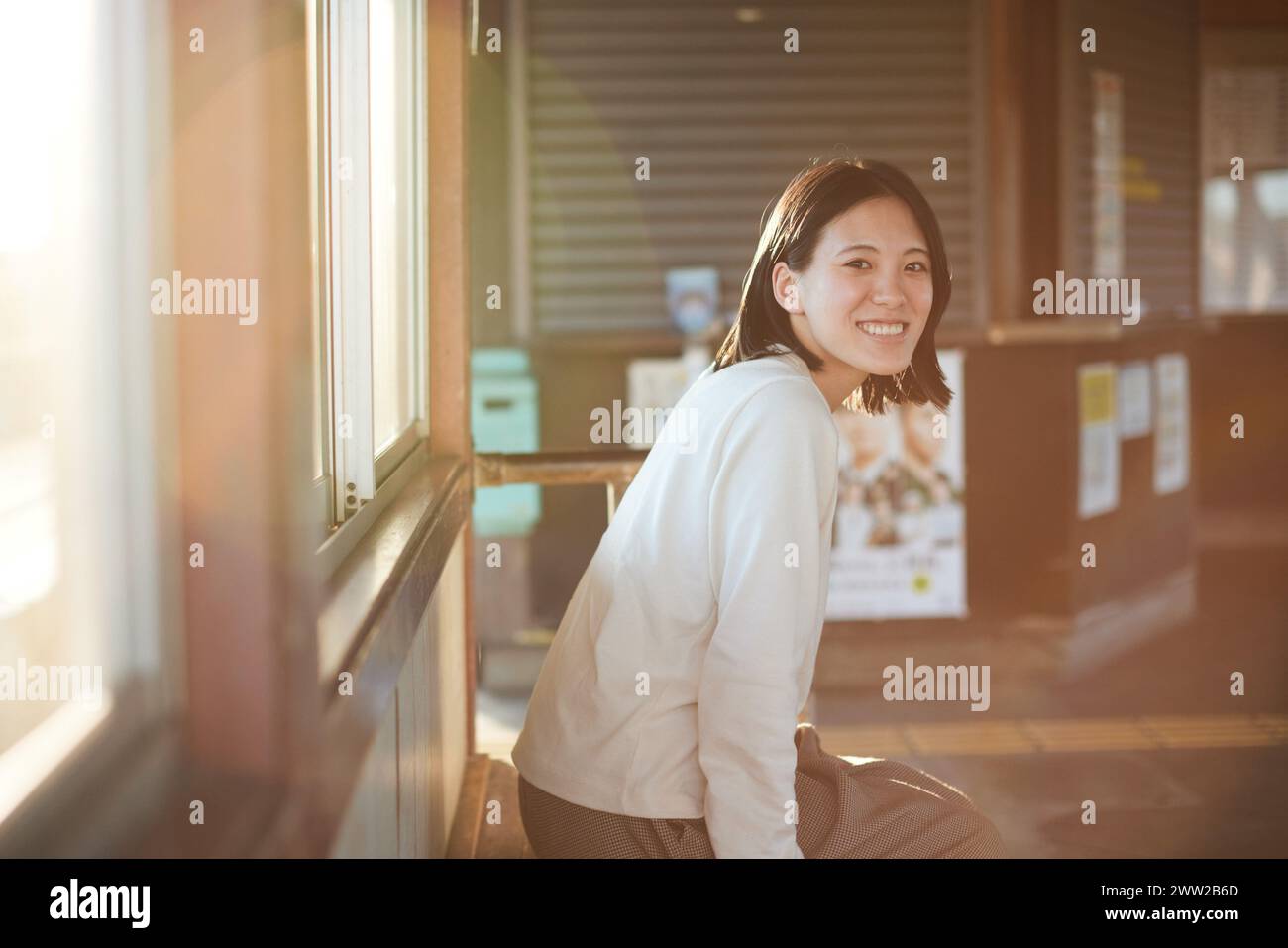 A woman sitting on a train platform with the sun shining through the ...