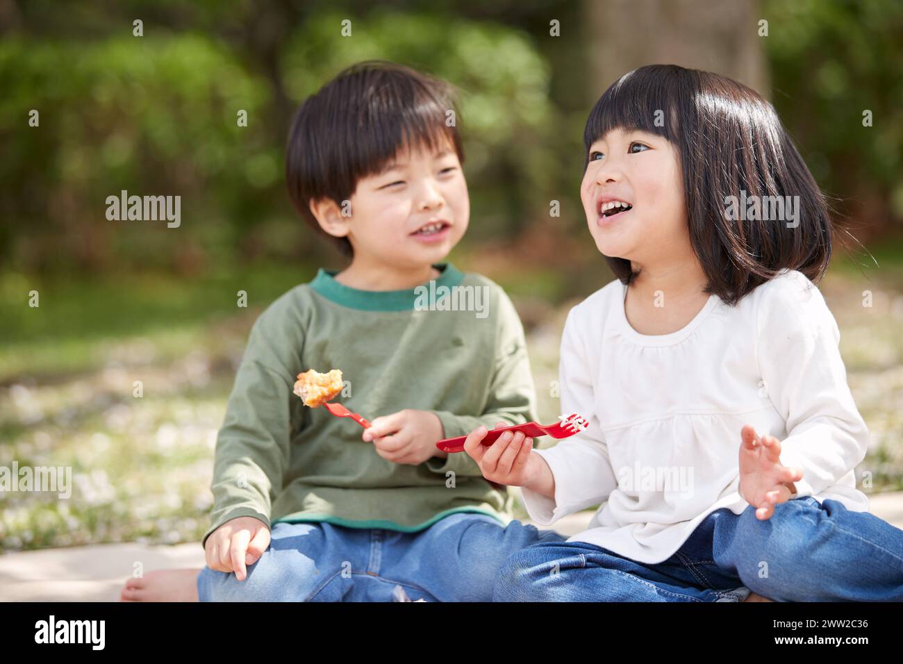 Two young children sitting on the ground eating Stock Photo - Alamy