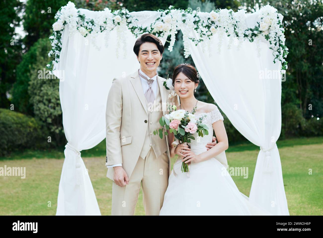 A newly married couple standing under a white wedding arch Stock Photo ...