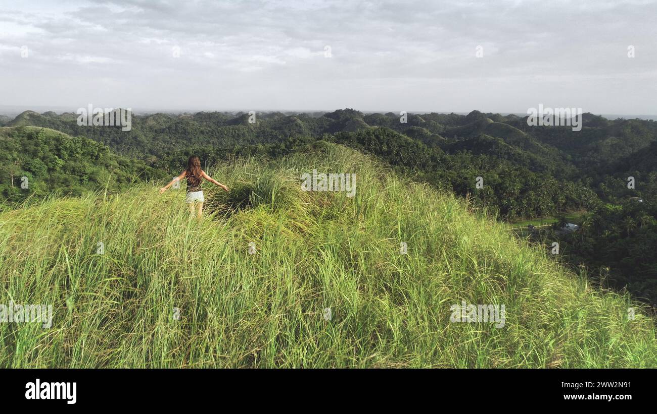 Woman rising up hands aerial view: green grass mount top in tropical ...