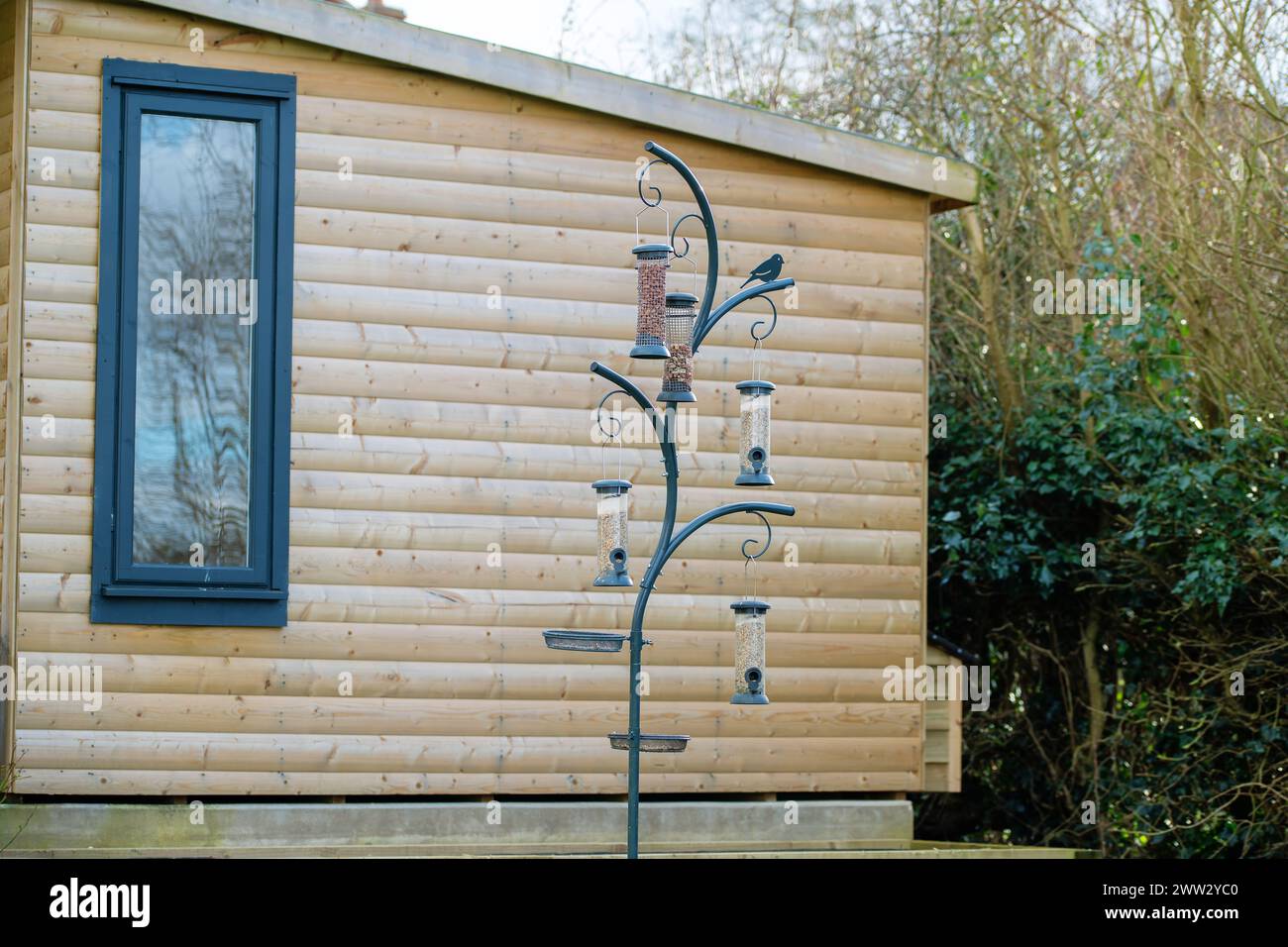 A curved bird feeding station with hanging bird feeders by the side of ...