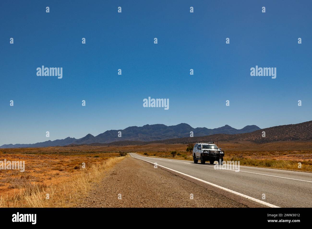 An SUV cruises along a remote outback road, mountains on the horizon ...