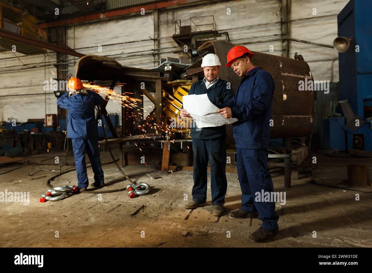 Engineer and worker consult over heavy machinery production, reviewing ...