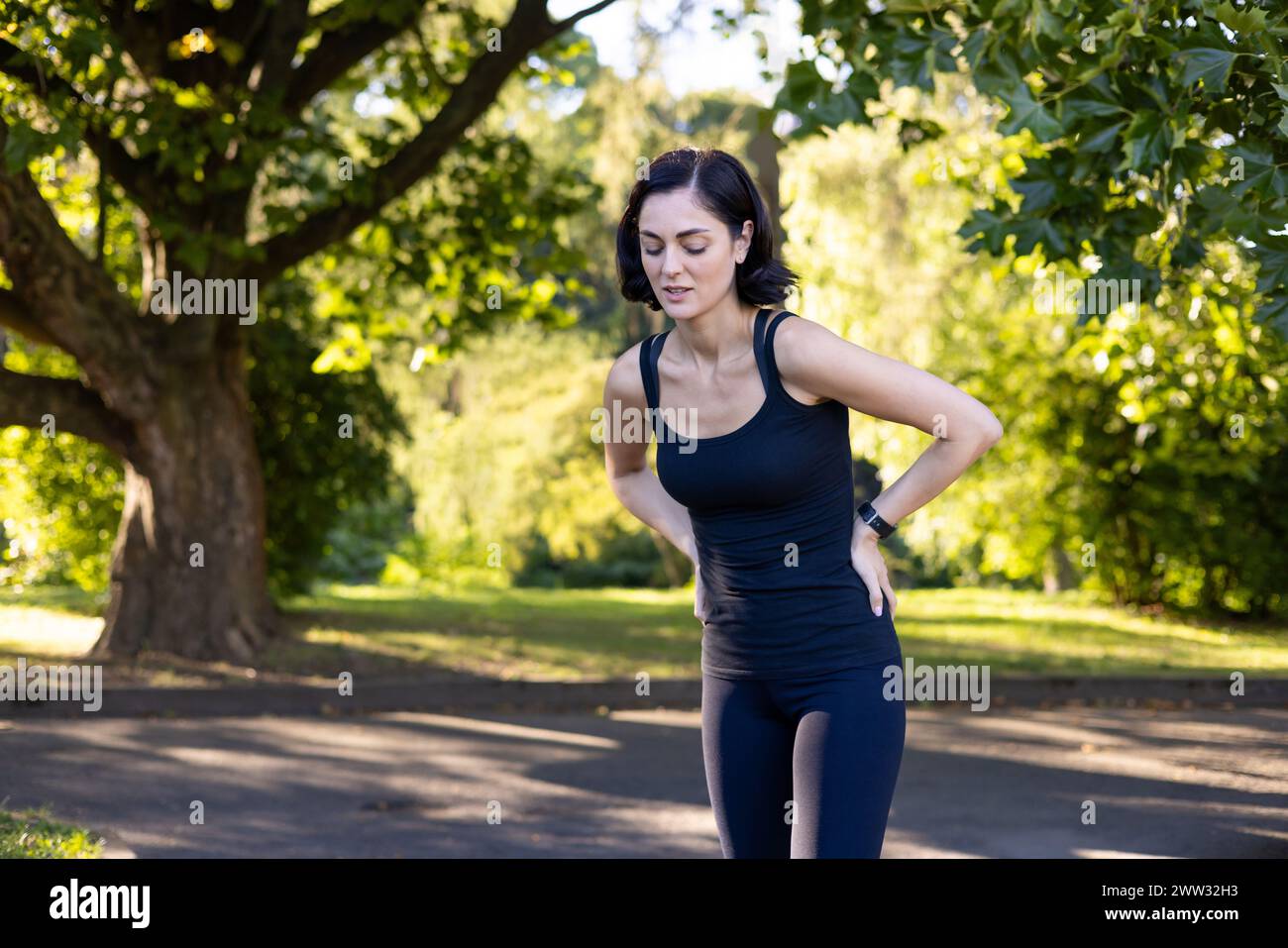 Active and sporty young woman standing in the park bent over, holding ...