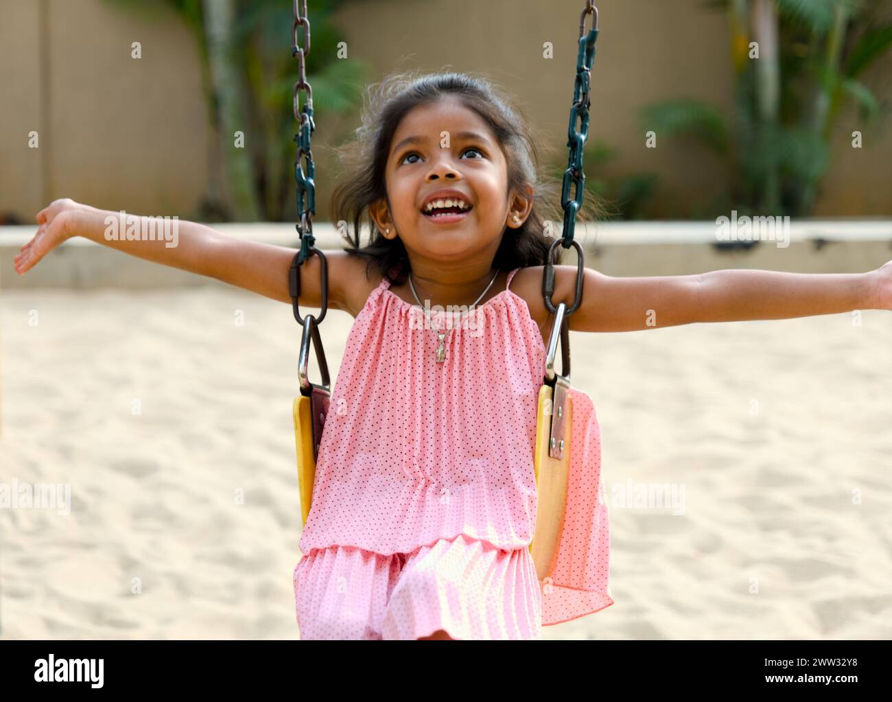 A carefree little girl with bright eyes laughs with glee as she pumps ...