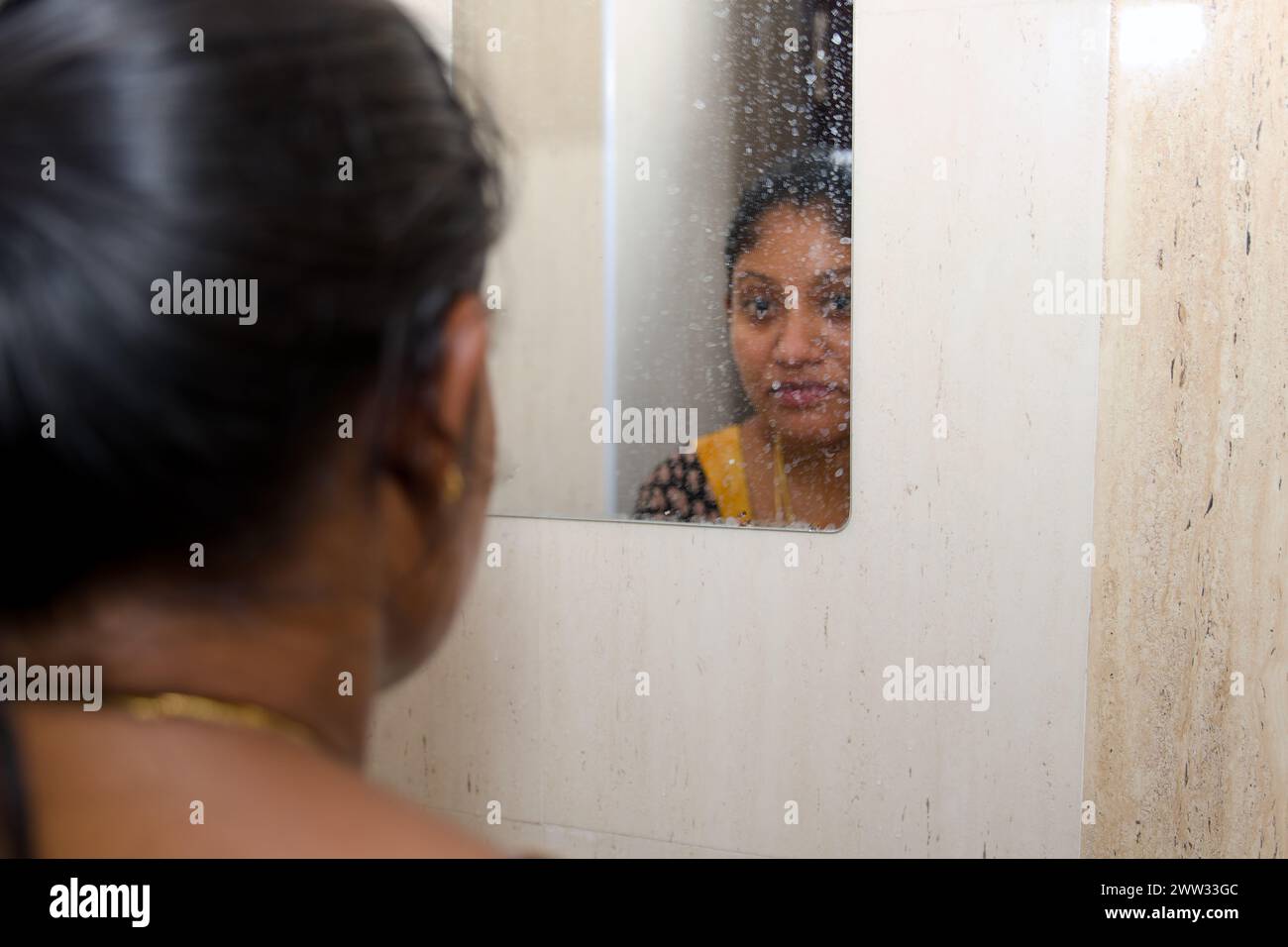 A woman gazes into a bathroom mirror, her reflection staring back Stock ...