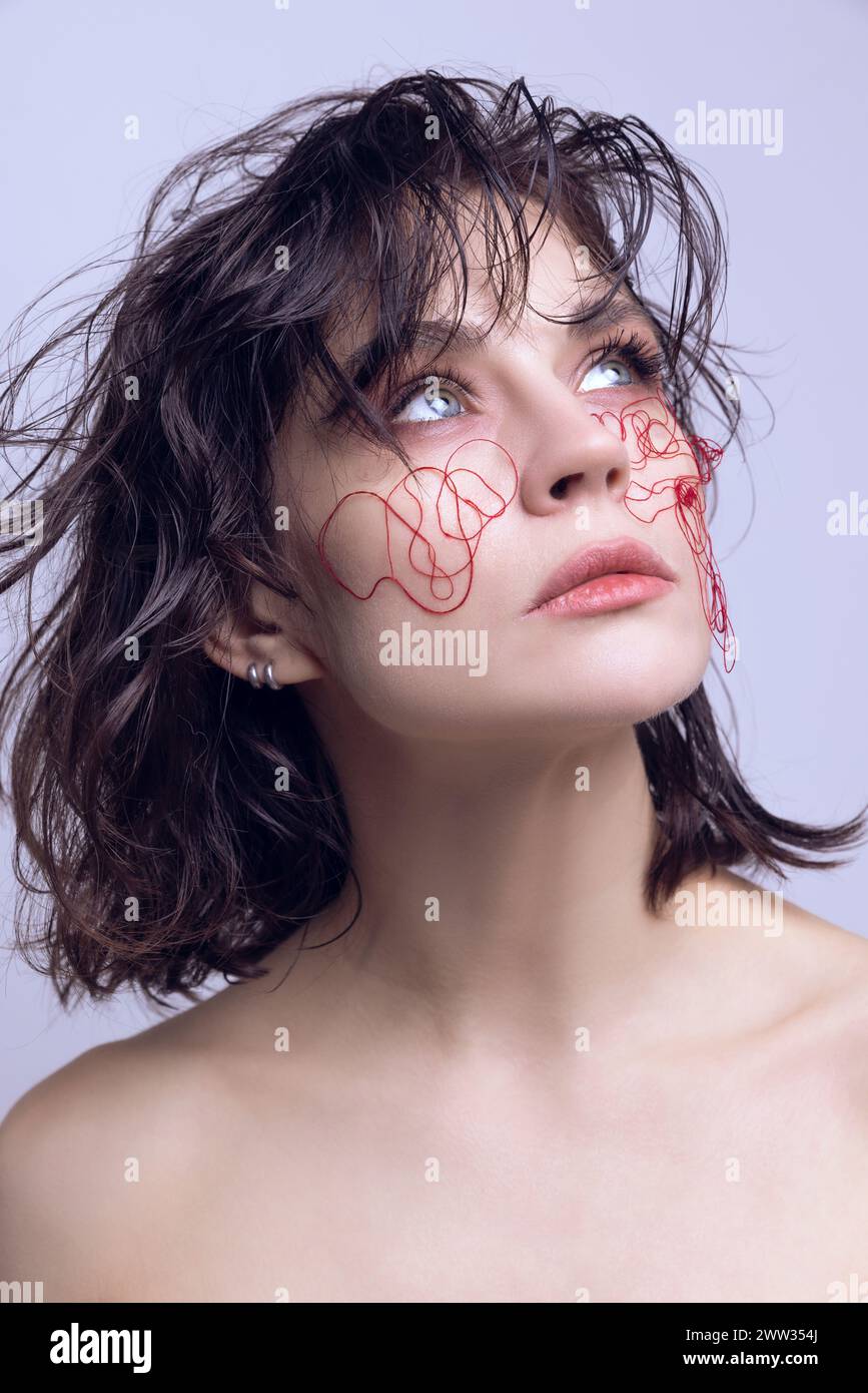 Beautiful young woman with tangled red strings on face, messy hair ...
