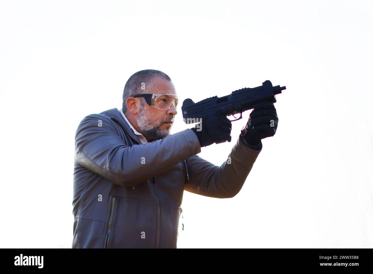 Man with gray jacket shooting black rifle aims at the target on a white ...