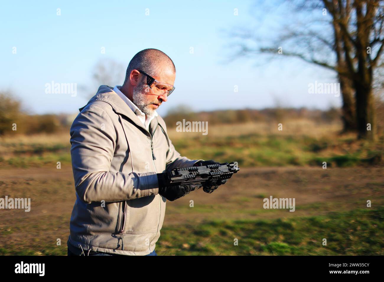 Man with gray jacket shooting black rifle on range Stock Photo - Alamy