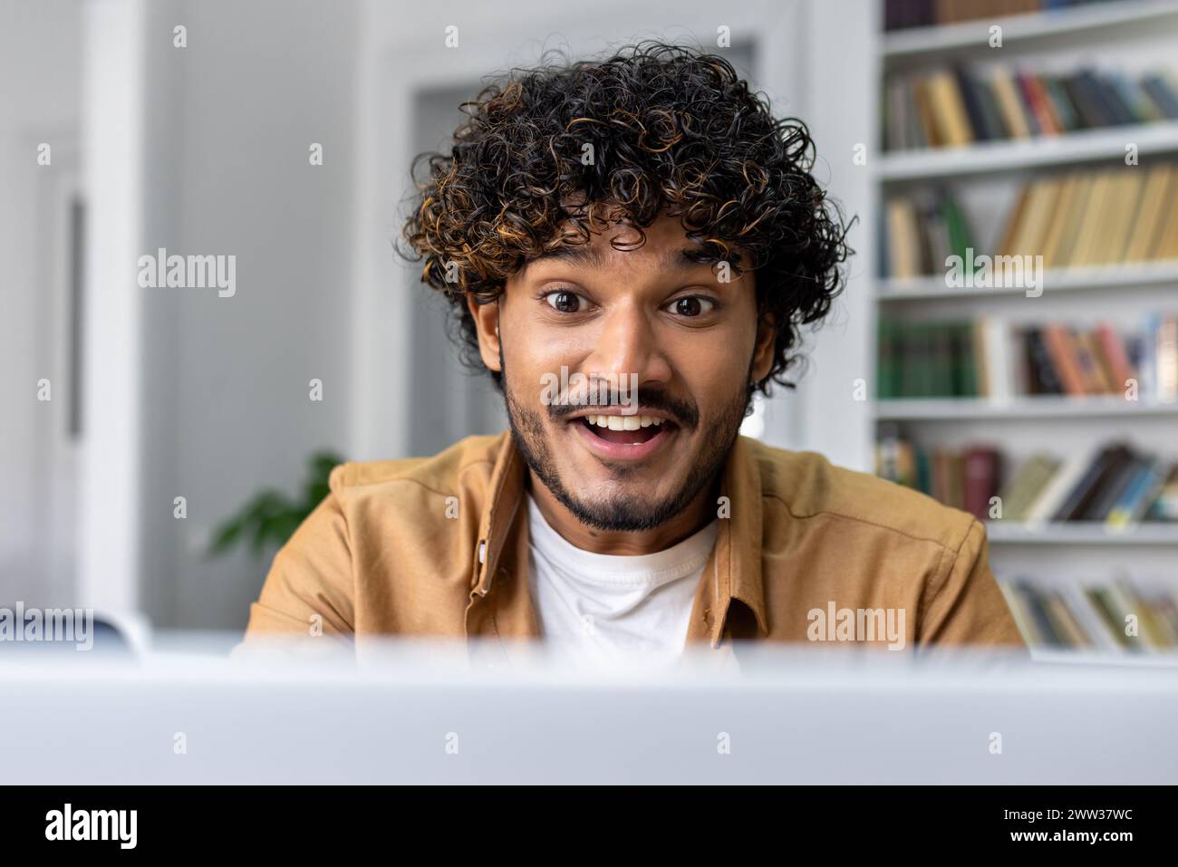A focused person sits in front of a computer in a well-lit home office ...