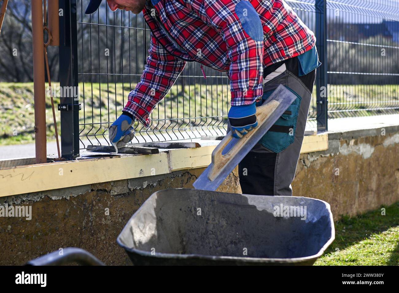 A man in overalls and gloves is repairing the fence in front of the ...