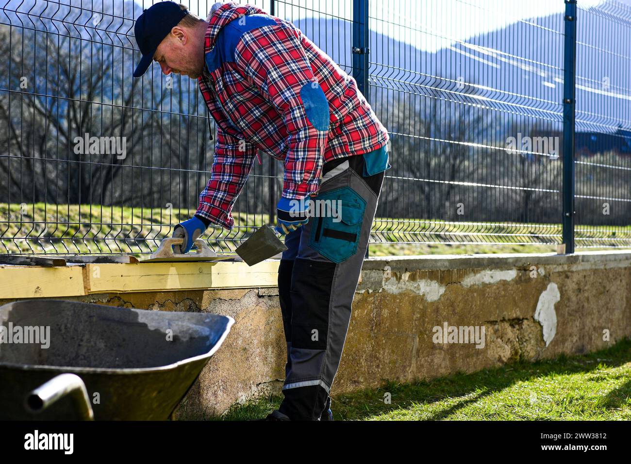 A man in overalls and gloves is repairing the fence in front of the ...