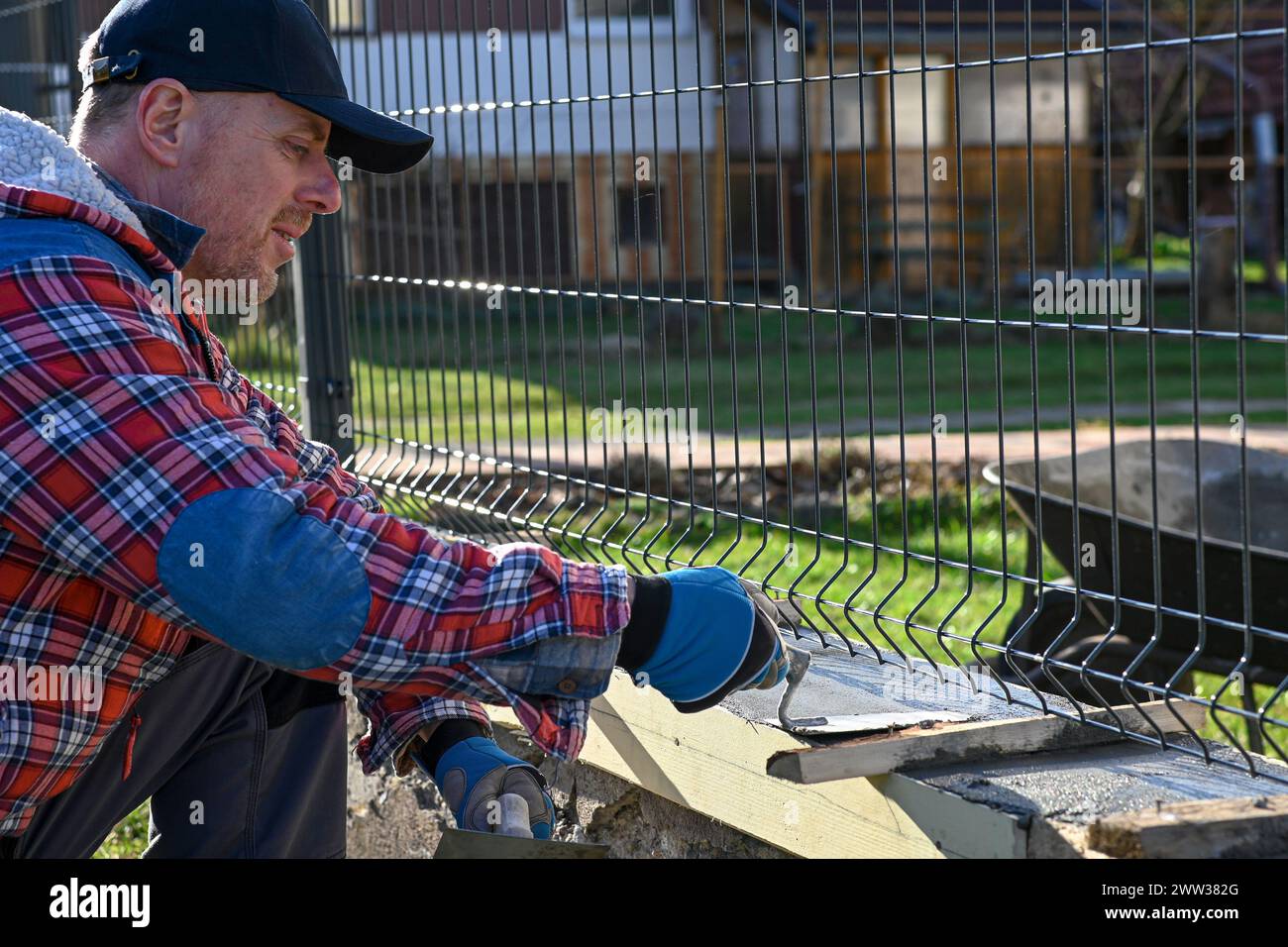 A man in overalls and gloves is repairing the fence in front of the ...