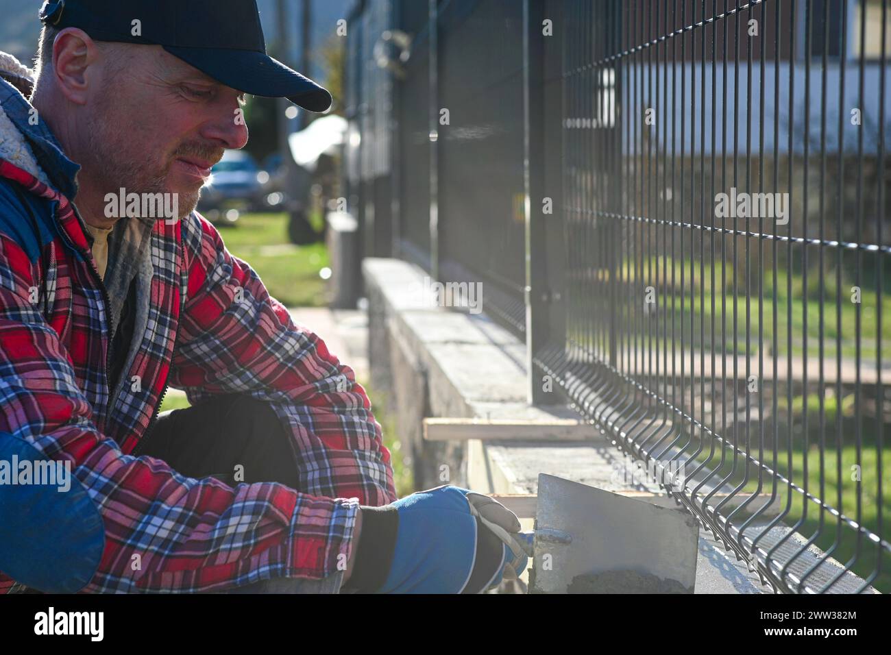 A man in overalls and gloves is repairing the fence in front of the ...