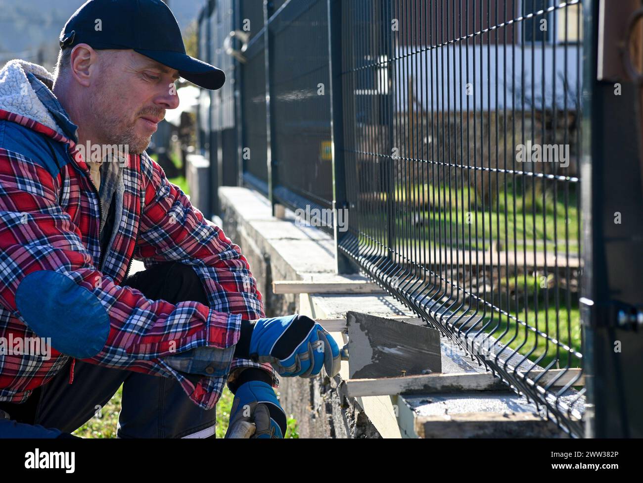 A man in overalls and gloves is repairing the fence in front of the ...
