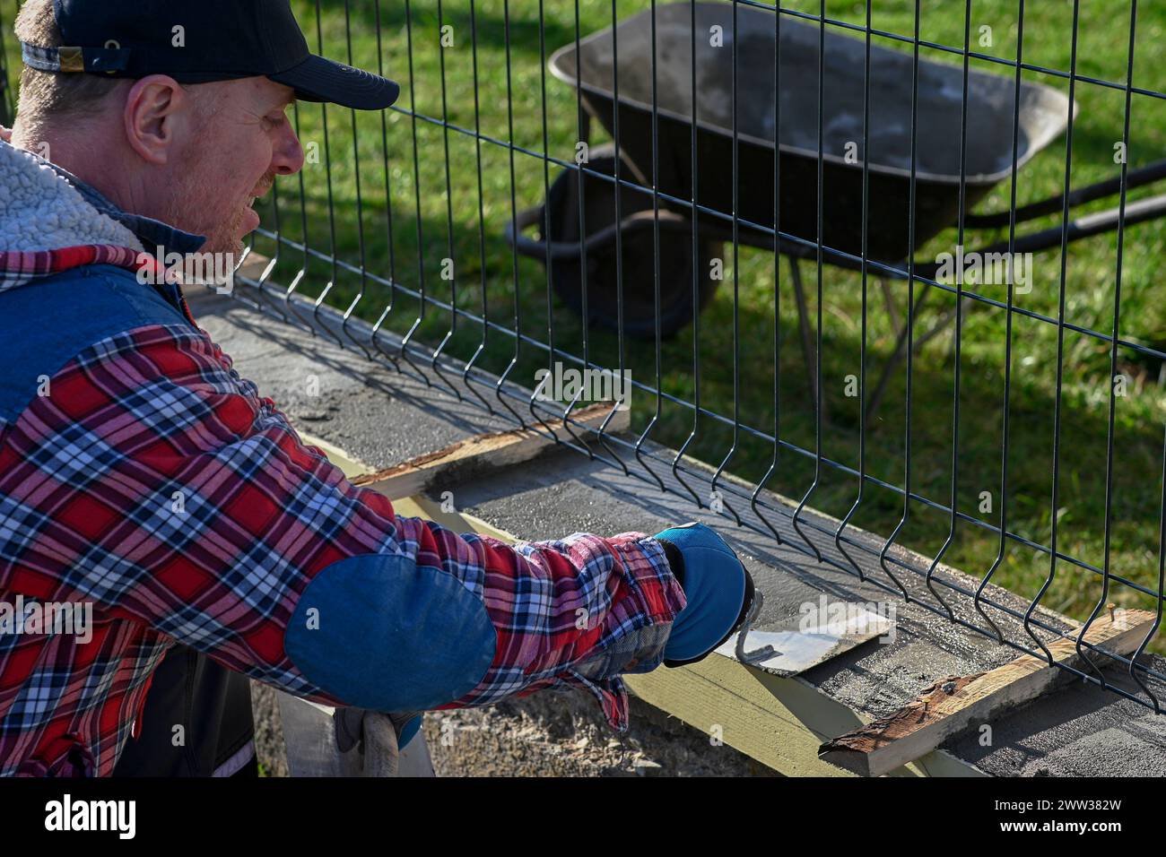 A man in overalls and gloves is repairing the fence in front of the ...