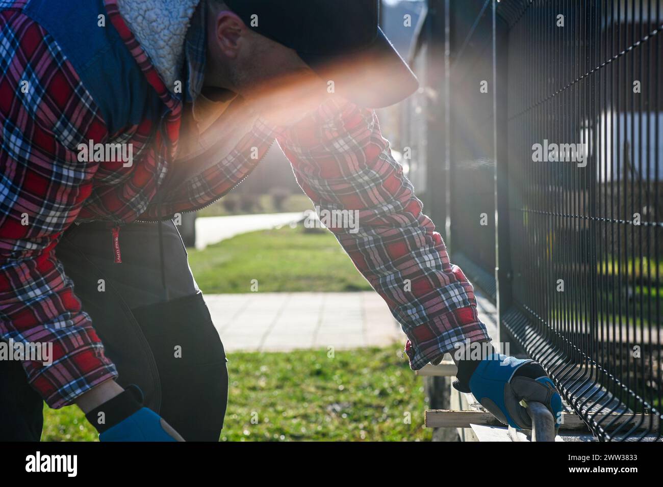 A man in overalls and gloves is repairing the fence in front of the ...