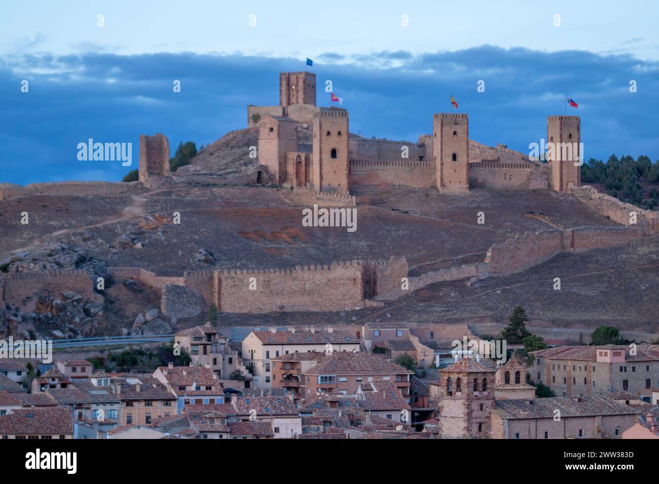 stone castle overlooks a quaint town, flags waving, under a soft ...