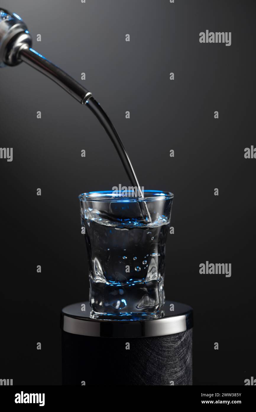 Vodka pouring from the bottle into a glass on a dark background. Blue ...