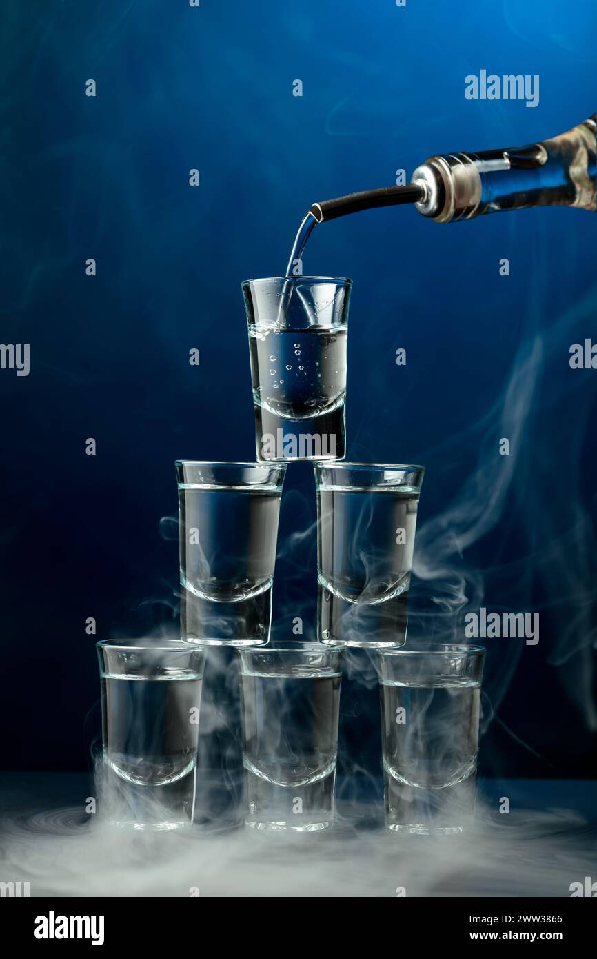 Vodka is poured from a bottle into a glass in smoke on dark blue ...