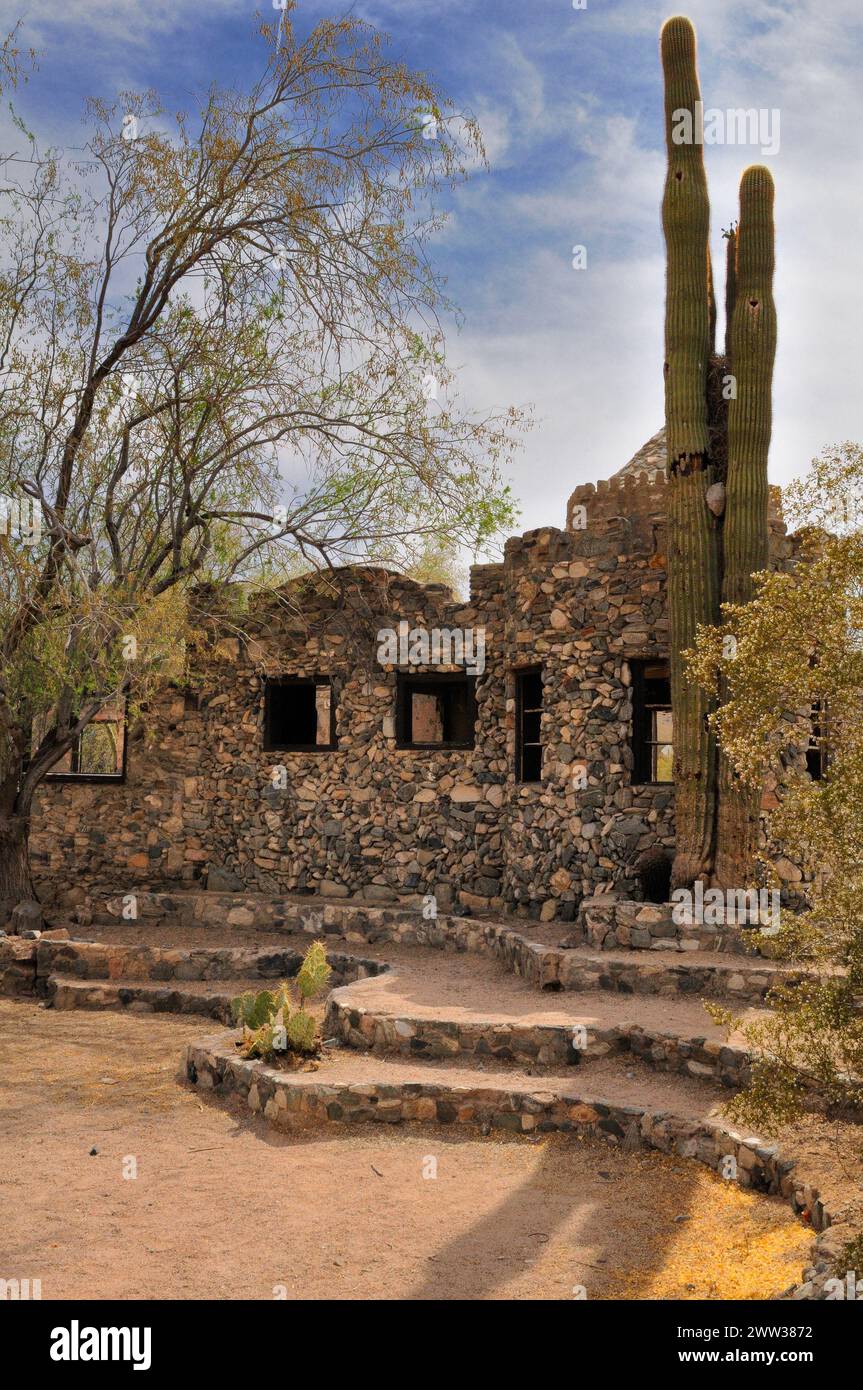 A weathered stone structure in the desert, surrounded by cacti and a ...