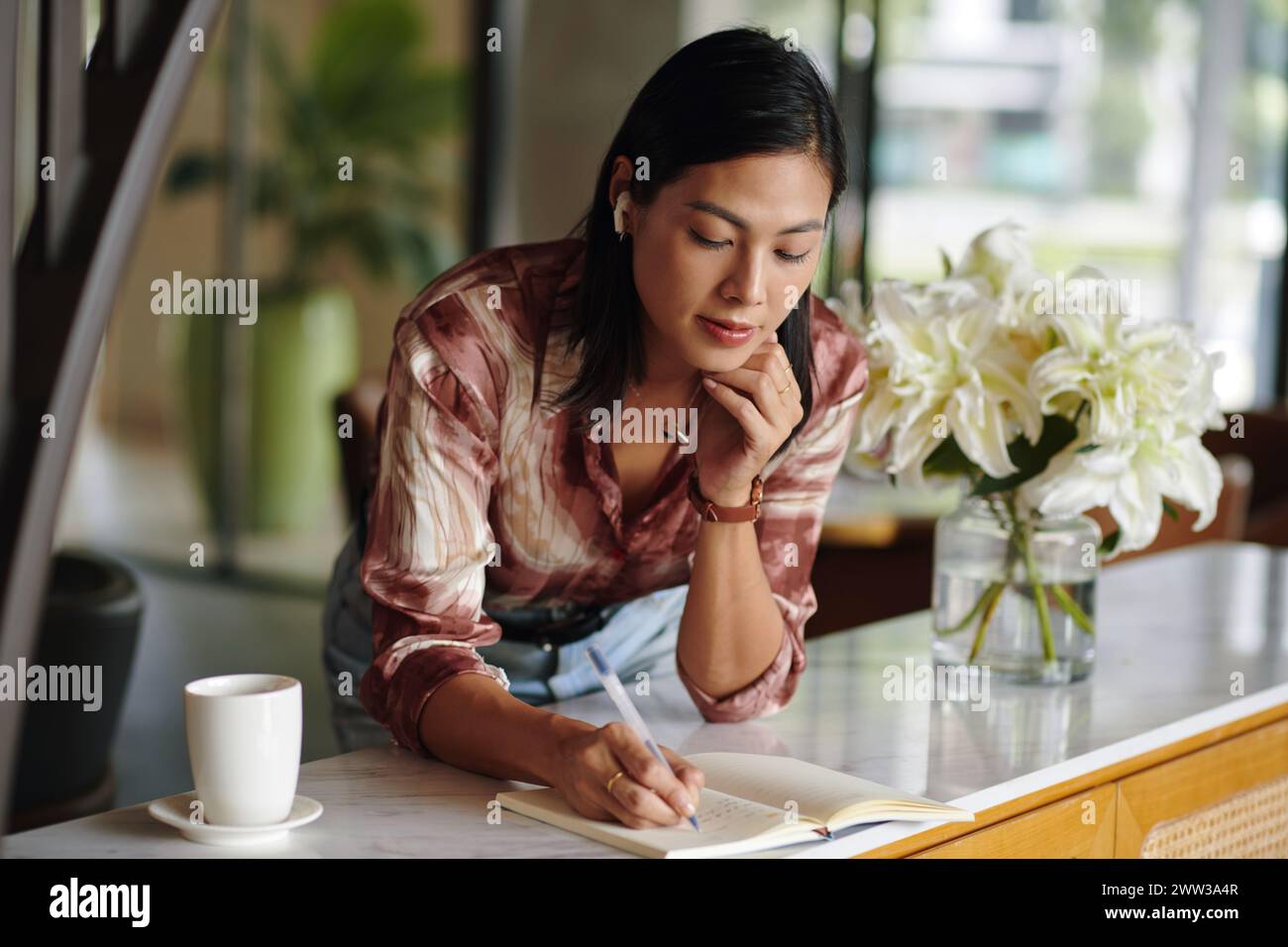 Pensive woman having morning coffee and writing down plans for the day ...
