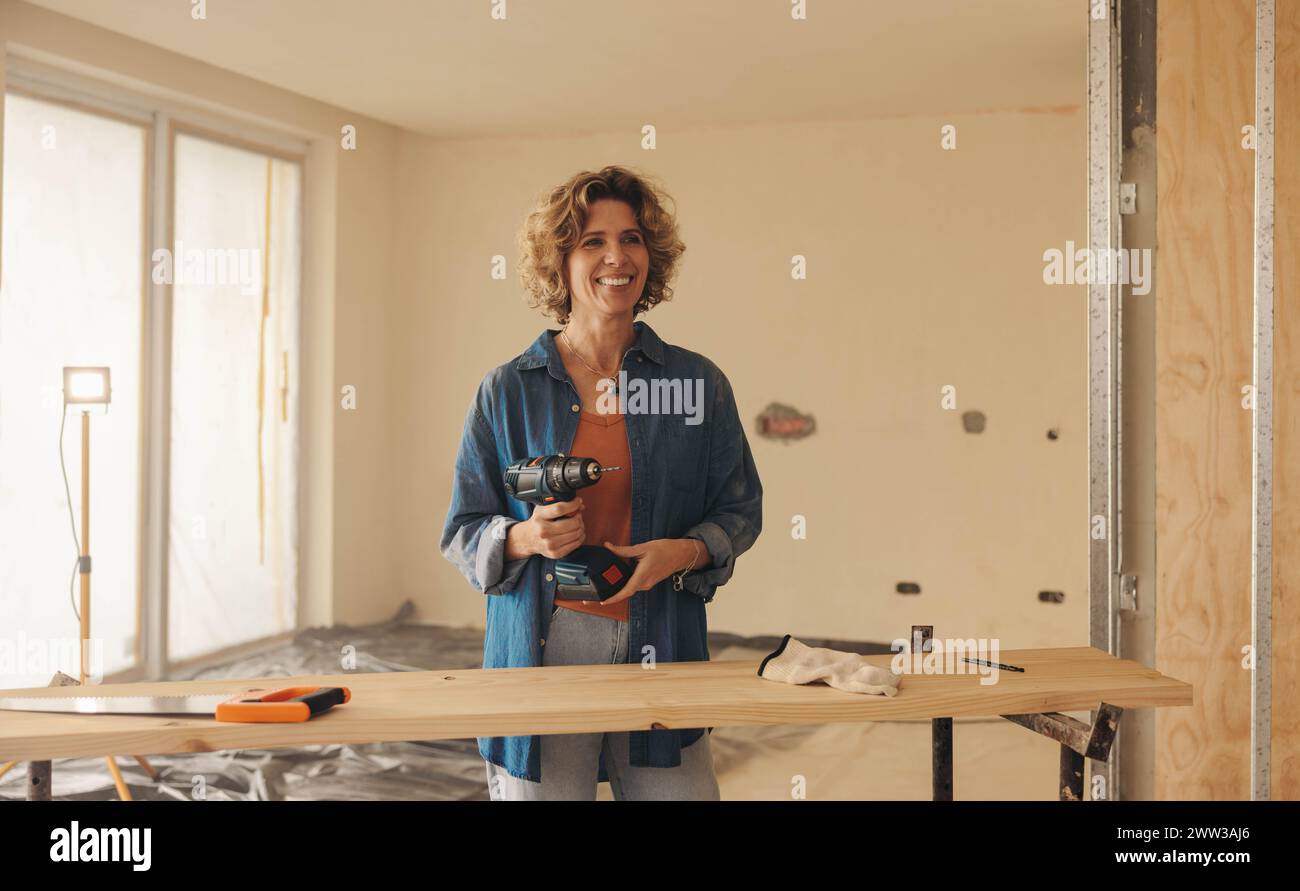 Happy female homeowner in her kitchen stands holding a drill gun ...