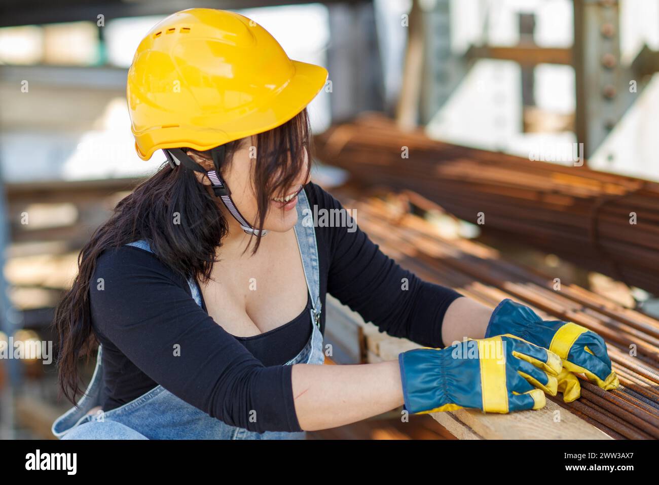Woman at work in retail building warehouse in hard hat and gloves examining metal beams with ...