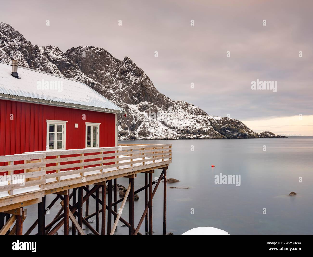 Traditional red wooden house on pegs by the fjord, snow-capped ...