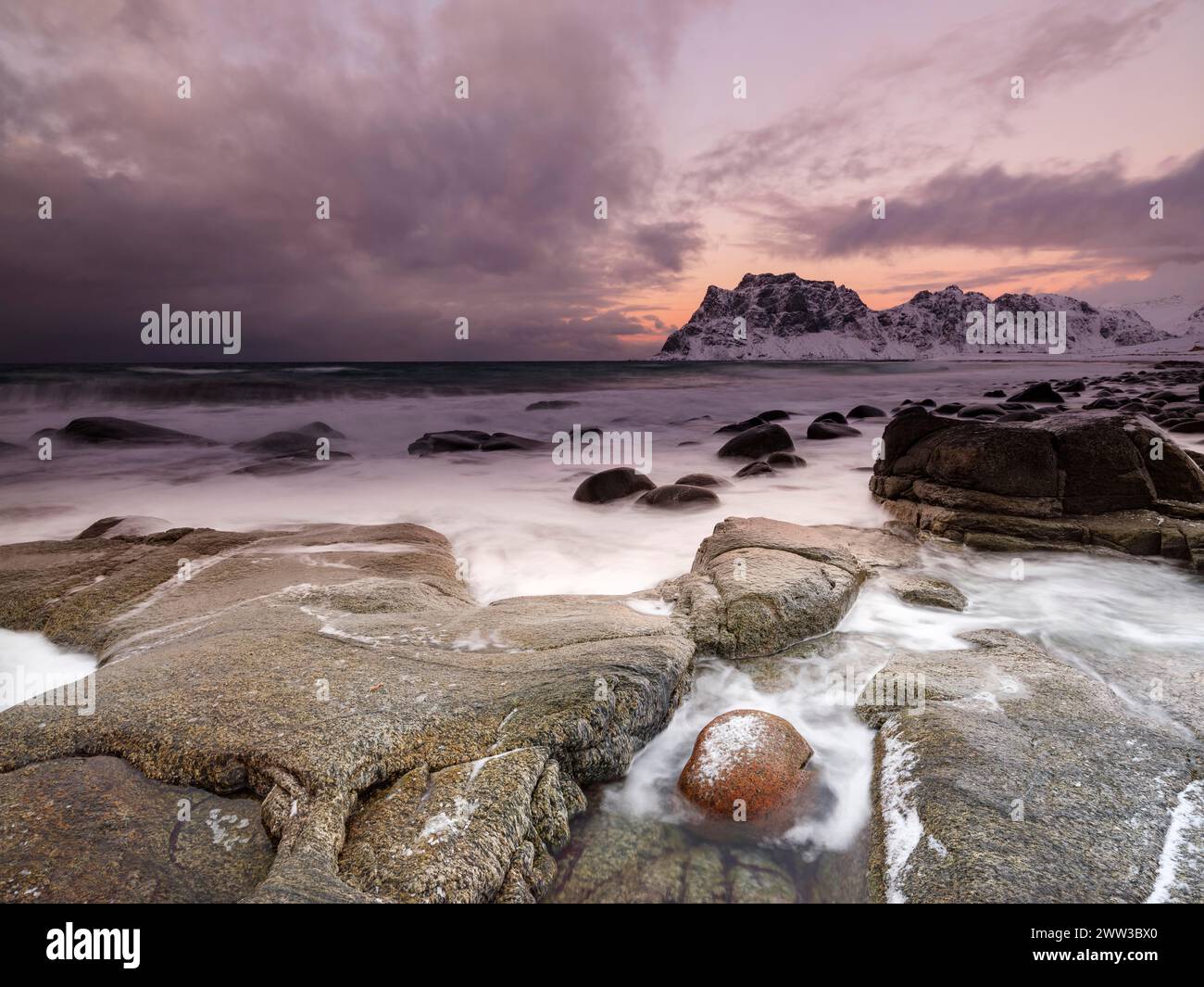 Rounded rocks on Utakleiv beach in a dramatic cloudy atmosphere, snow ...
