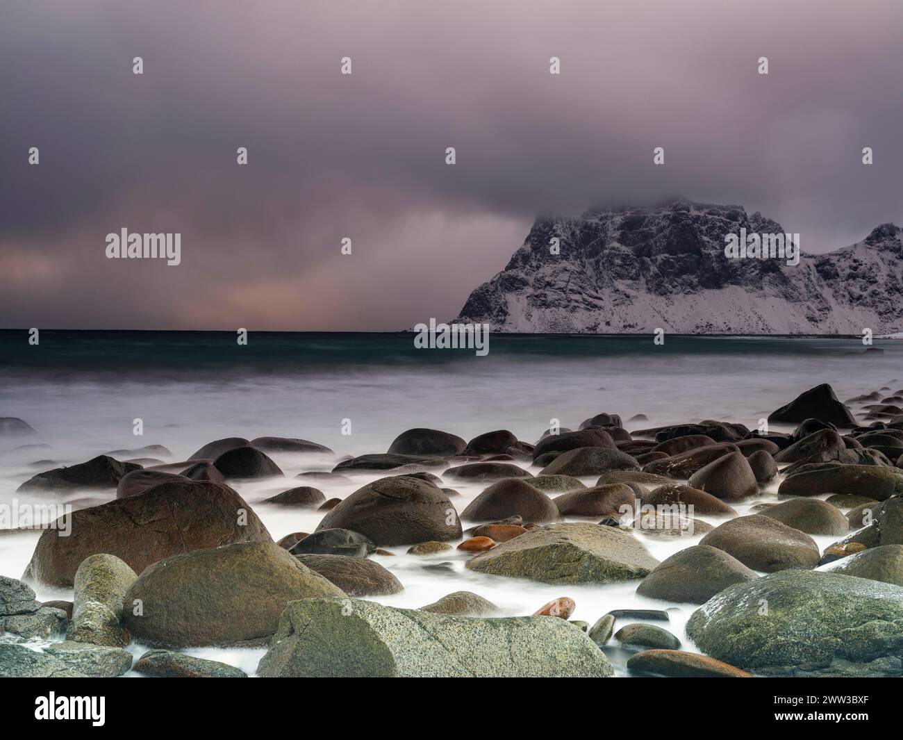 Rounded rocks on Utakleiv beach in a dramatic cloudy atmosphere, snow ...