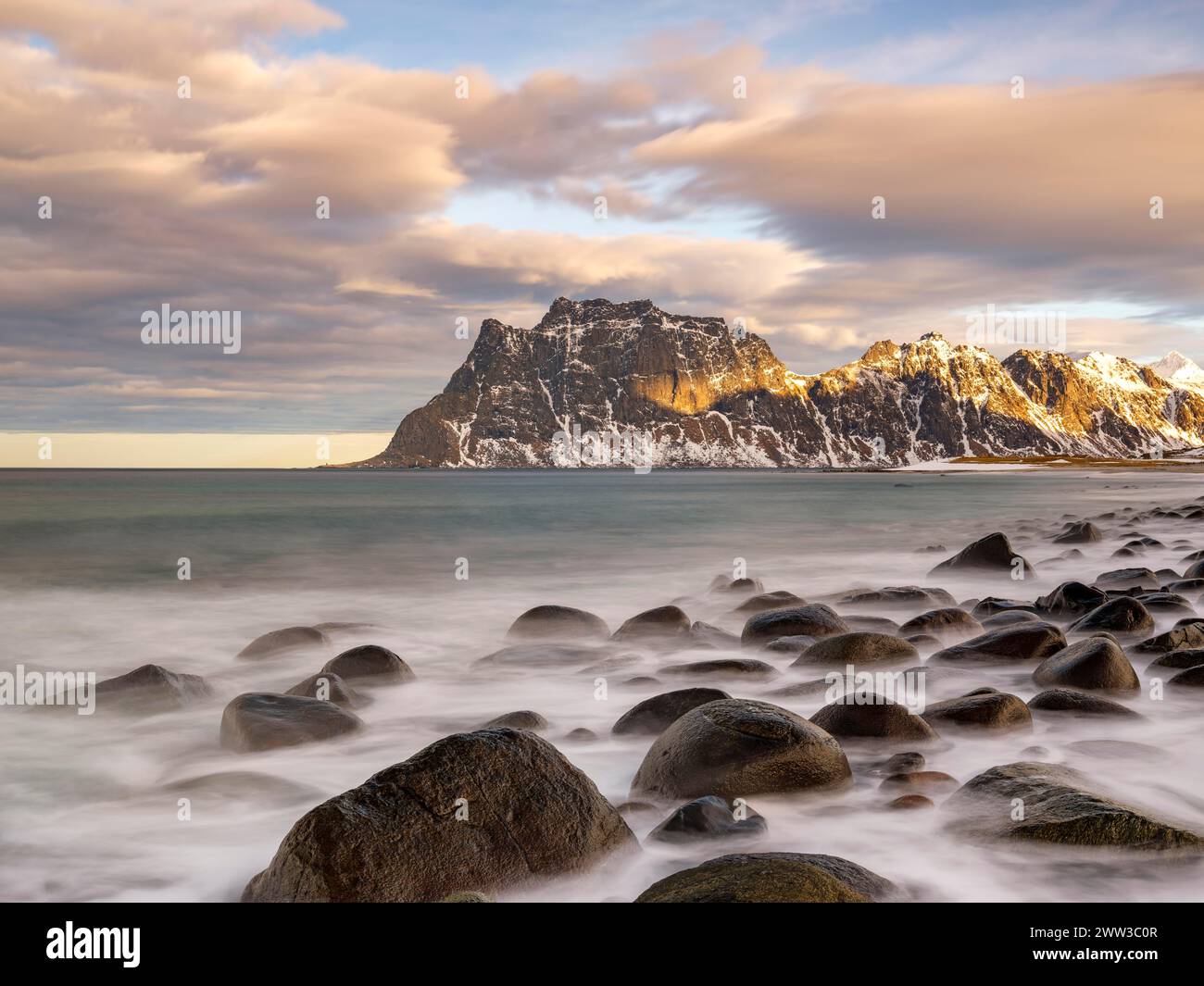 Rounded rocks on Utakleiv beach in a dramatic cloudy atmosphere, snow ...