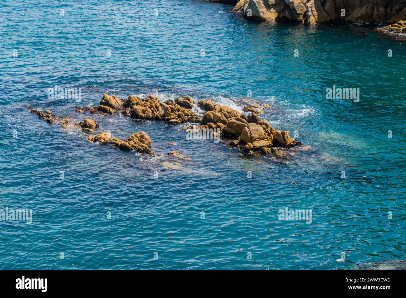 A rocky outcrop in the midst of blue ocean waters on a clear day, in ...