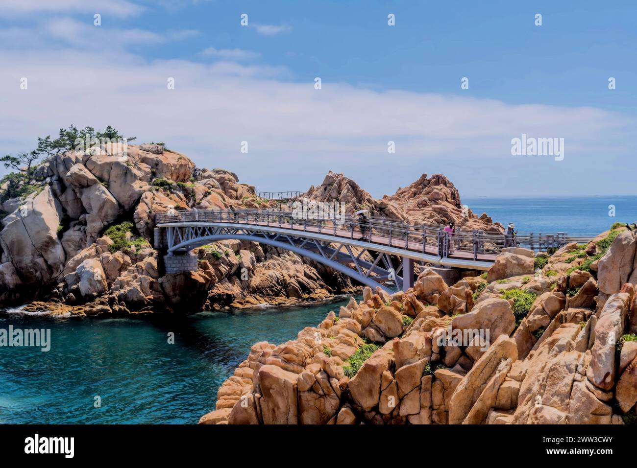 A bridge spanning over rocks by the sea with a clear blue sky, in Ulsan ...