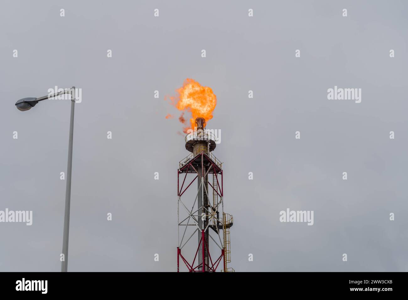 Flaring gas burns at the top of an industrial stack against a gloomy ...