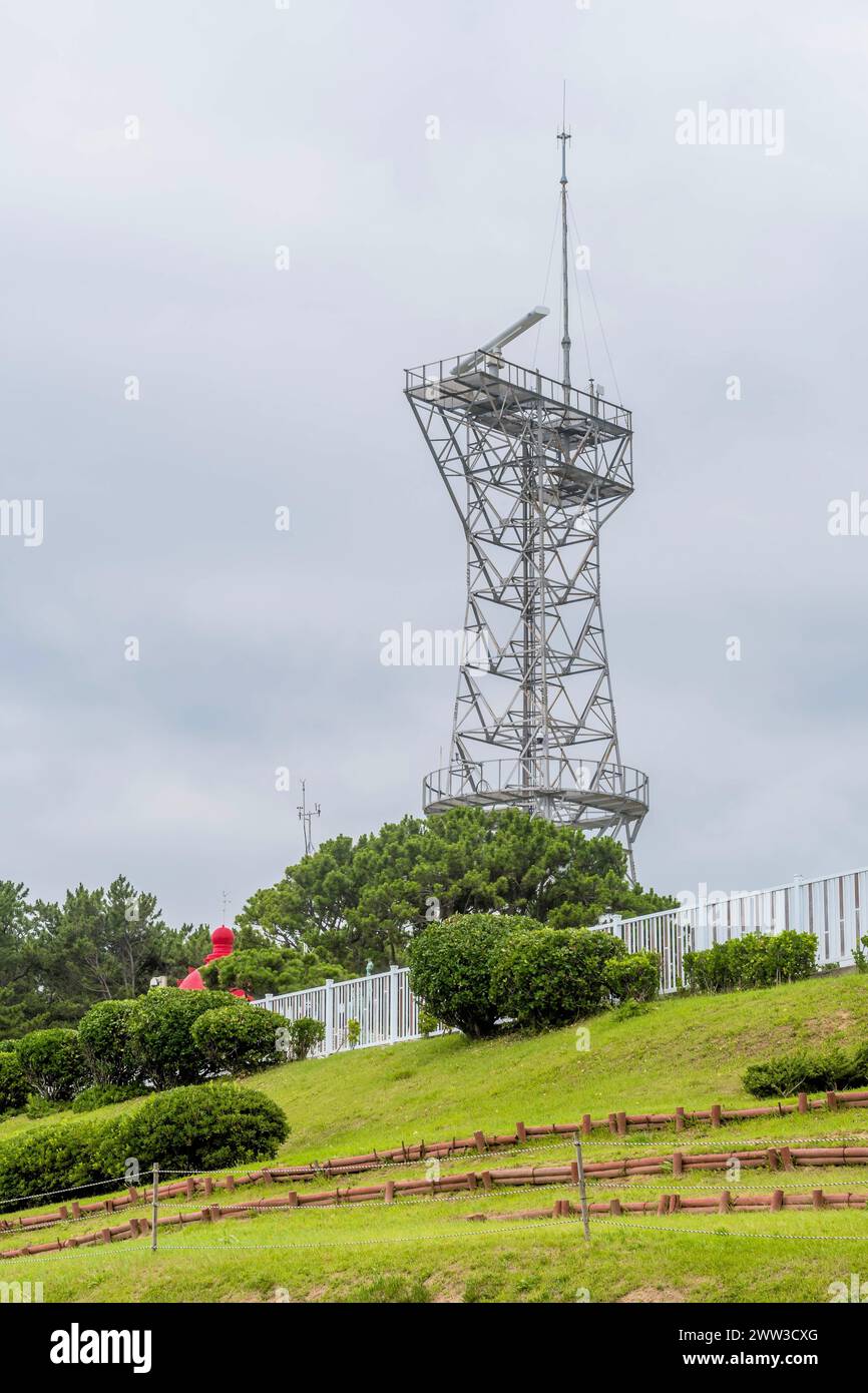 Tall metal radar tower standing amidst lush greenery under a cloudy sky ...