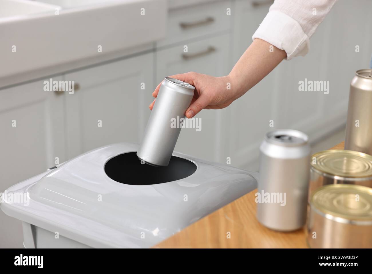 Garbage sorting. Woman throwing metal can into trash bin indoors ...
