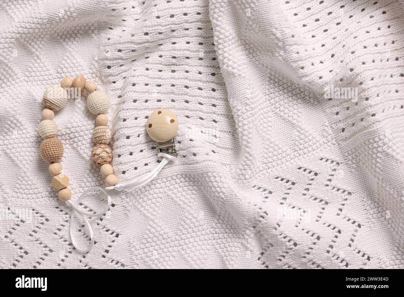 Baby accessory. Pacifier clip on white knitted fabric, top view. Space ...