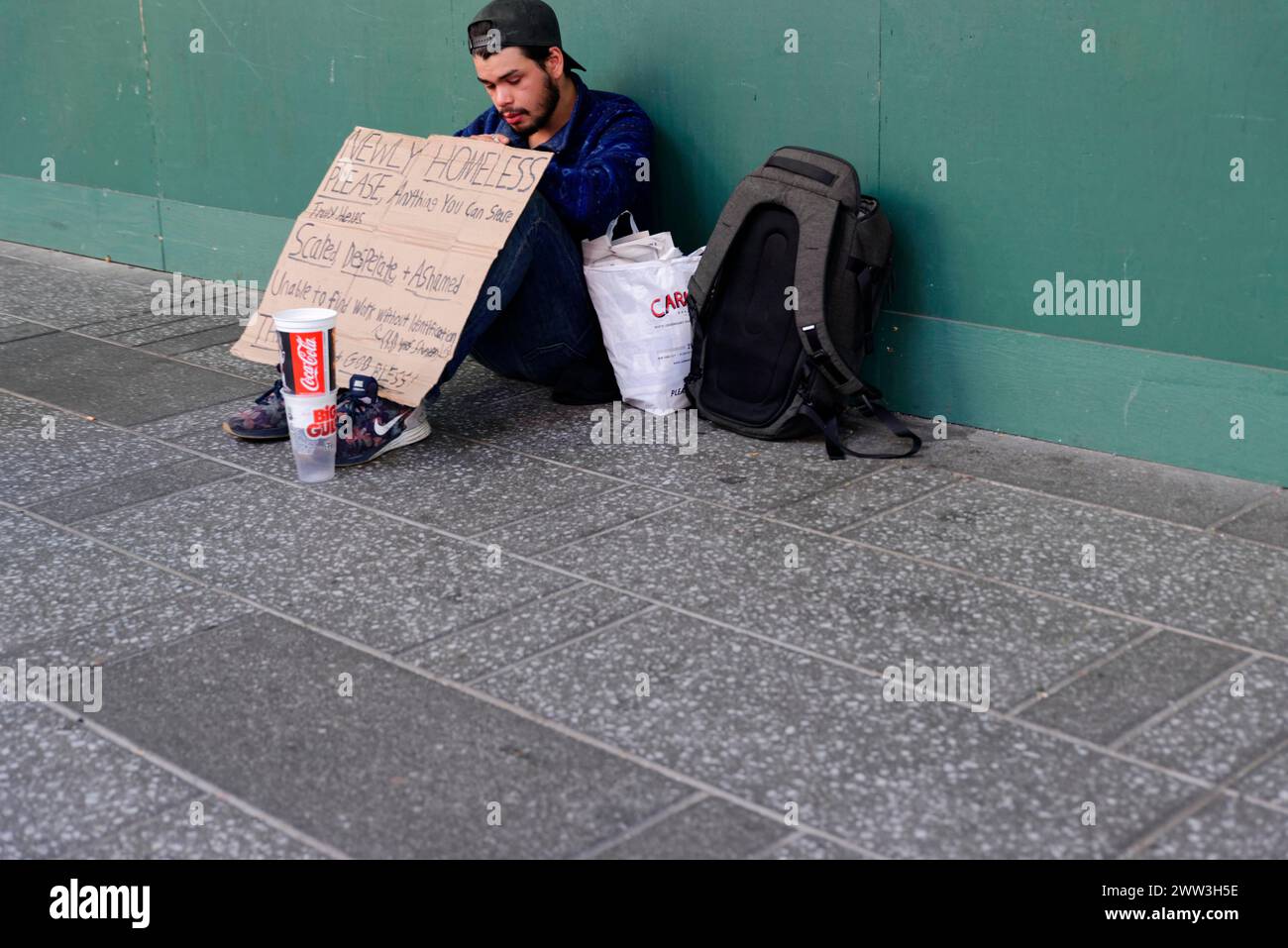 A homeless man sits on the pavement with a sign asking for help ...