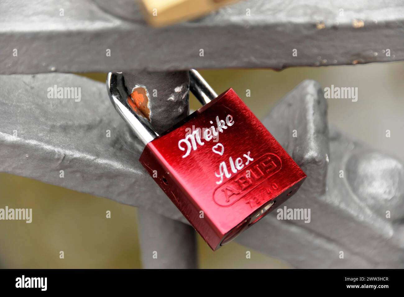 A red love lock with engraved names attached to a metal railing ...
