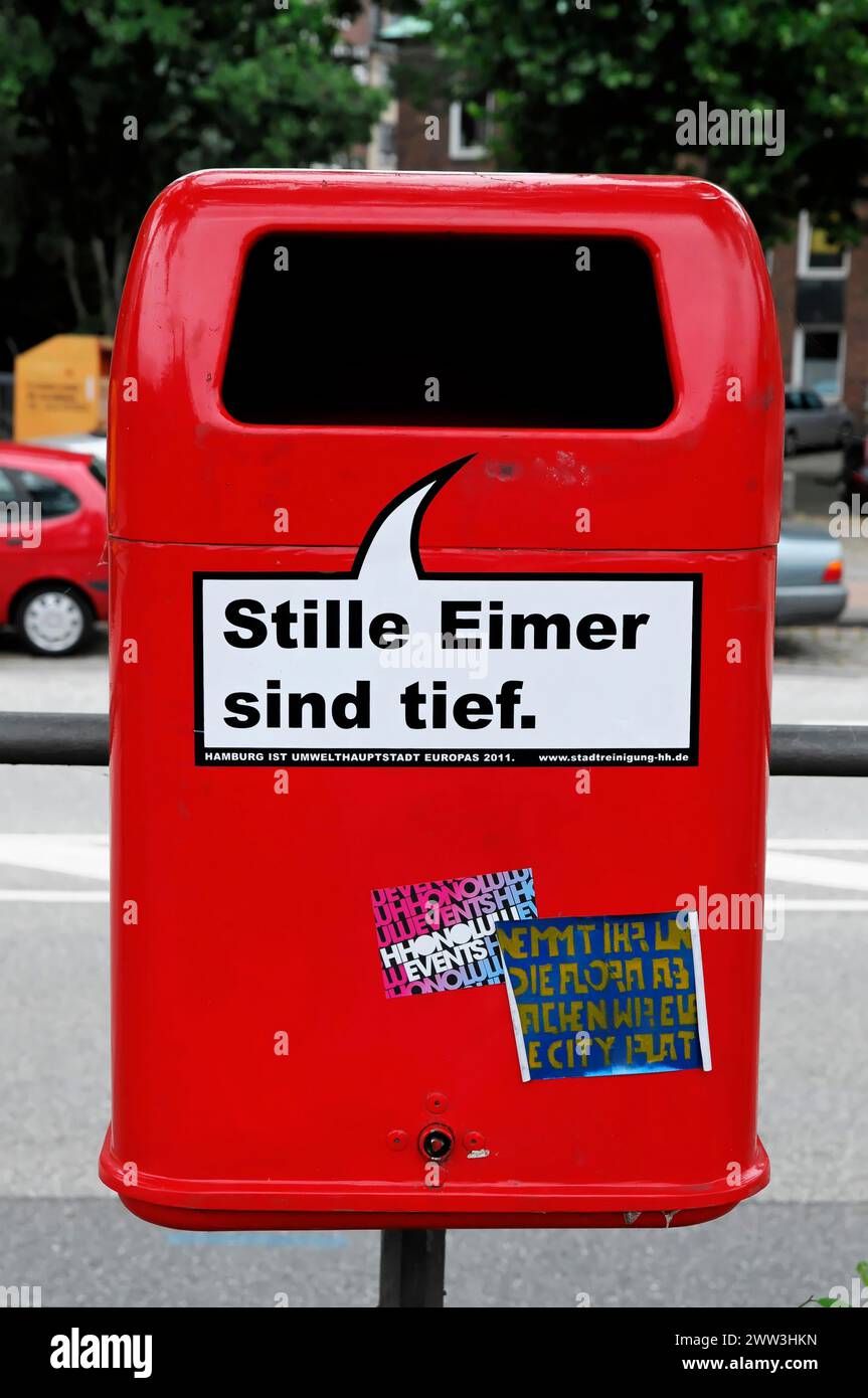A bright red rubbish bin with stickers in front of a blurred city ...