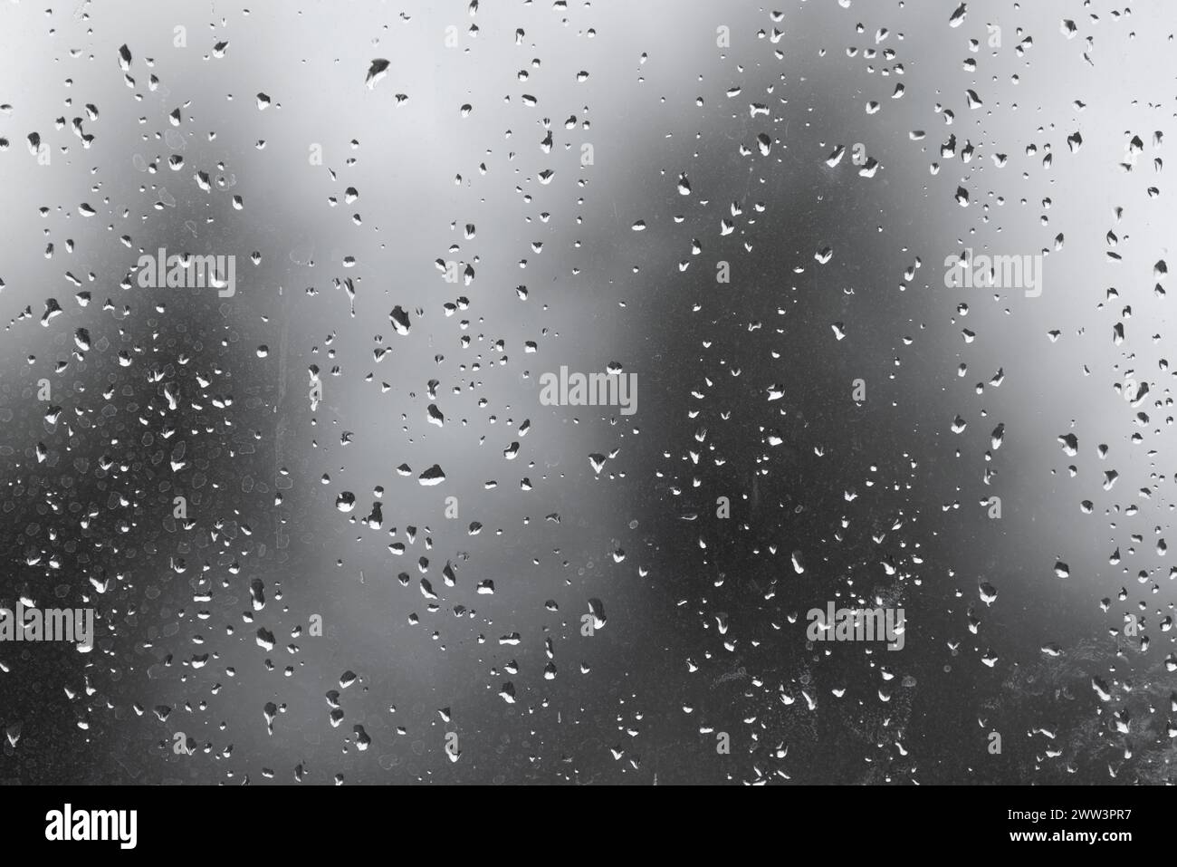 Dirty wet window glass with droplets and gray blurred environment behind, rainy photo background ...