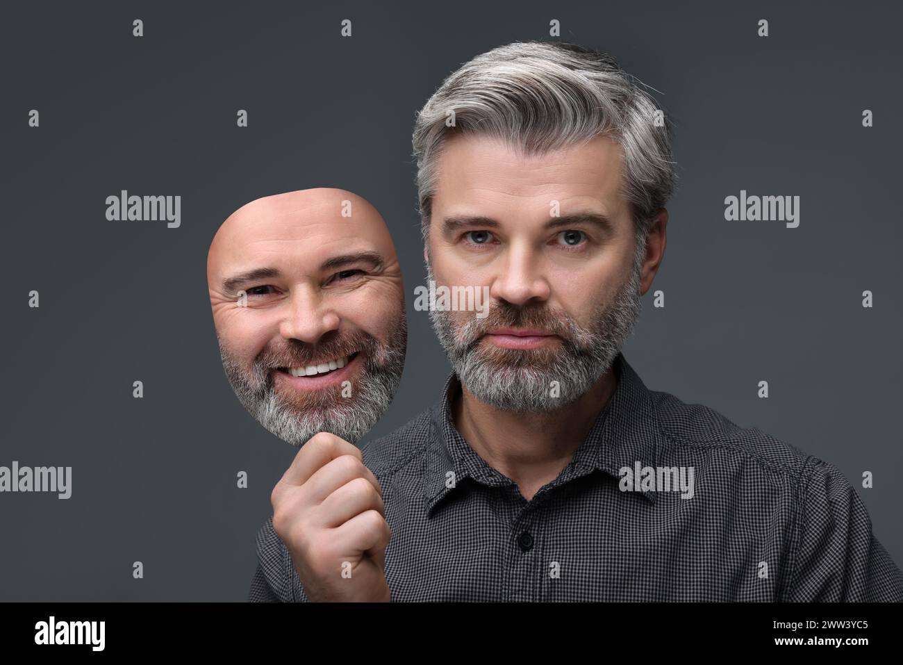 Man holding mask with his facial expression on grey background ...