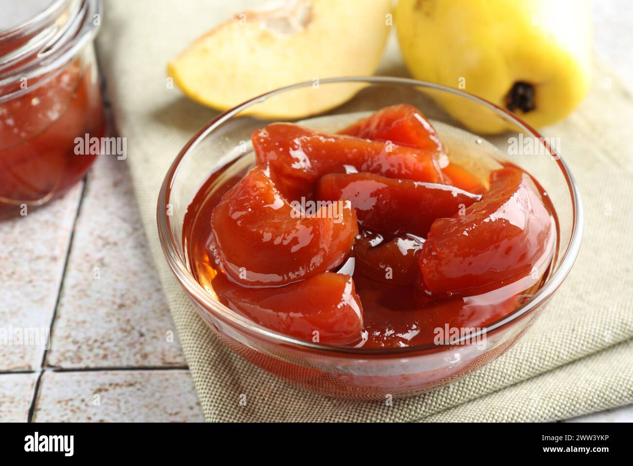 Tasty homemade quince jam in bowl and fruits on tiled table, closeup ...