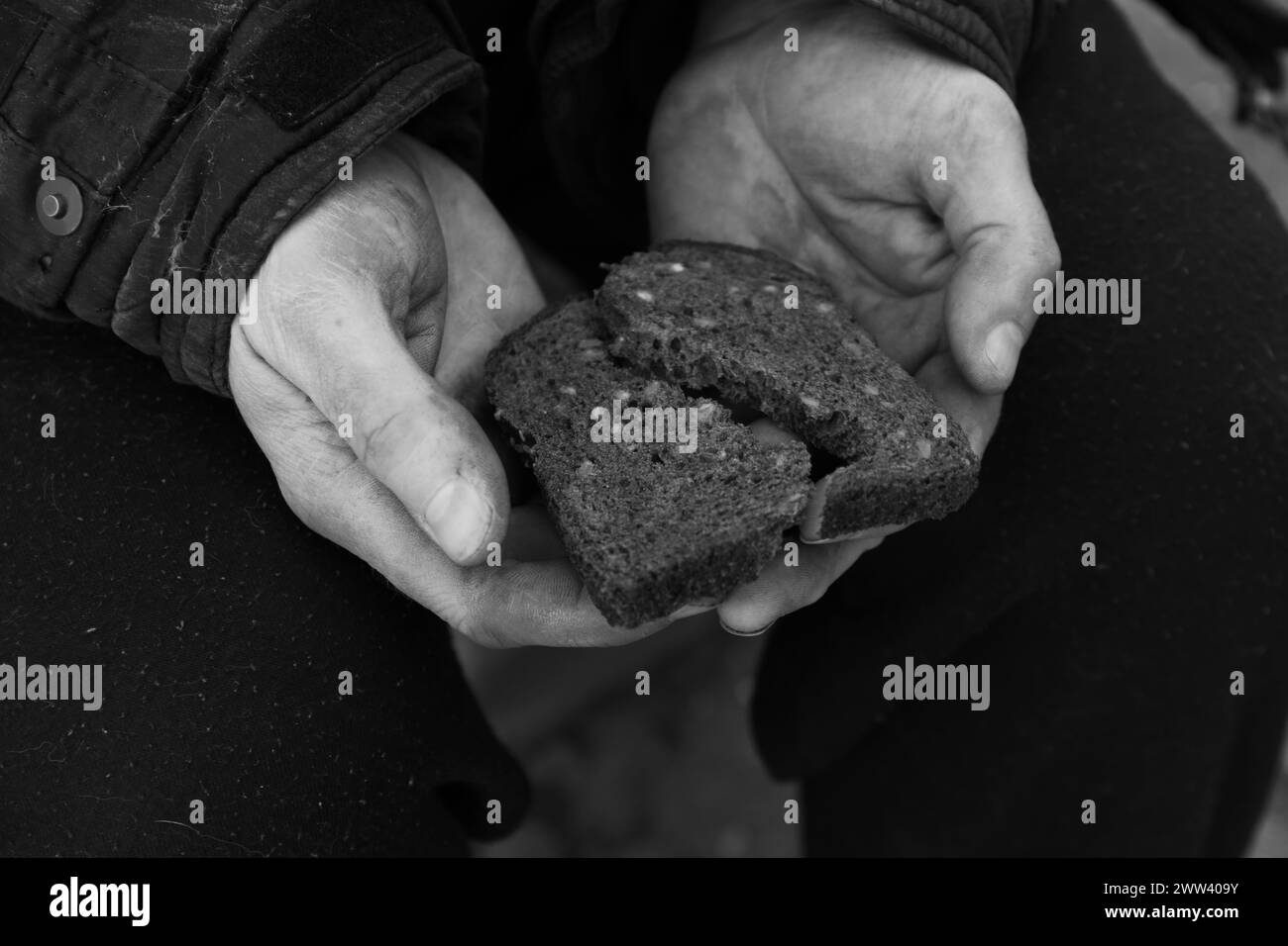 Poor homeless man holding piece of bread outdoors, closeup. Black and ...