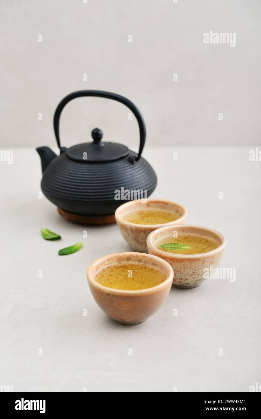 Black cast iron teapot and three ceramic cups of green tea on a light ...